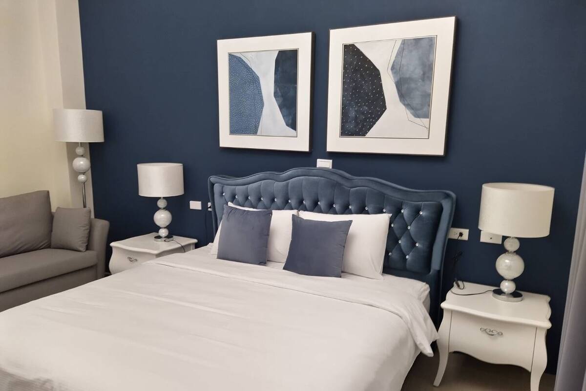 Quarto bem arrumado com uma cama grande, duas mesas de cabeceira, um criado-mudo, uma luminária e um sofá.