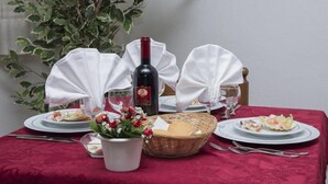 Mesa posta para refeição com guardanapos brancos, uma garrafa de vinho, uma cesta e um vaso de planta.