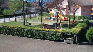 Um parquinho com balanços e escorregadores, cercado por um viveiro e árvores.