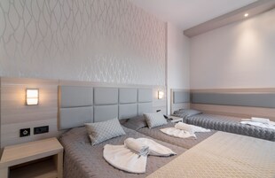 Quarto de hotel moderno com uma cama grande, mesa de cabeceira e luminária fixada na parede.