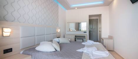 Quarto de hotel moderno com uma cama grande, mesas de cabeceira, toucador com espelho e televisão de ecrã plano na parede.