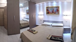 Quarto de hotel moderno com uma cama grande, um guarda-roupa, uma escrivaninha com cadeira e uma mesinha.