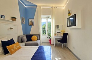Quarto de hotel moderno com cama, escrivaninha, cadeira e televisão fixada na parede.