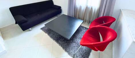 Uma sala de estar moderna com um sofá preto, uma mesa de centro cinza e duas cadeiras vermelhas.
