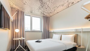 Quarto de hotel com cama, escrivaninha, cadeira, janela e teto com padrão único.