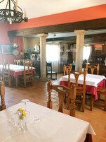 Uma sala de jantar de hotel com mesas e cadeiras de madeira, um candelabro e vista para a entrada do hotel.