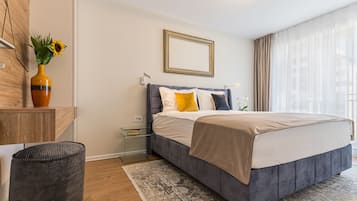 Quarto moderno com cama, mesa de cabeceira, abajur e uma janela grande com cortinas.