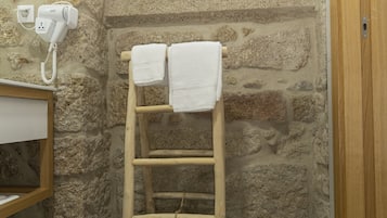 Um banheiro com parede de pedra, escada de madeira com toalhas, uma janela e um secador de cabelo branco na parede.