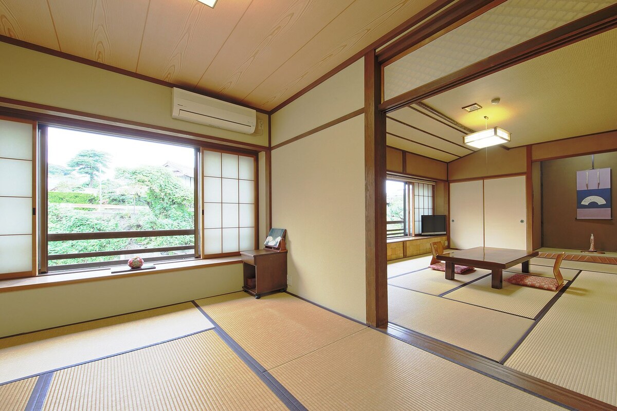 Um quarto japonês tradicional com tatames, portas deslizantes, uma televisão e uma mesa pequena.