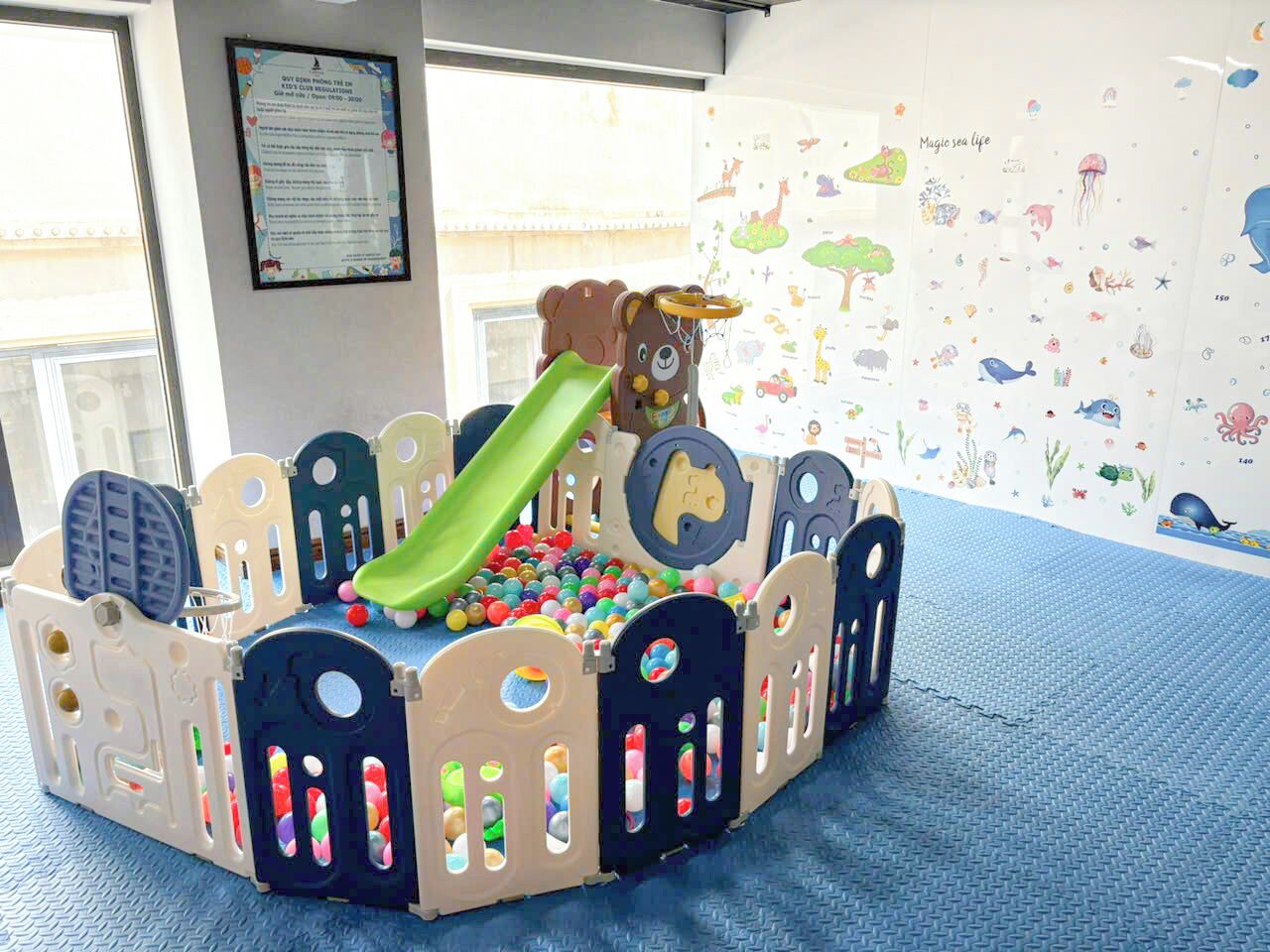 Área de recreação infantil com escorregador e piscina de bolinhas, cercada por uma grade de proteção.