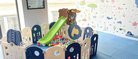 Área de recreação infantil com escorregador e piscina de bolinhas, cercada por uma grade de proteção.