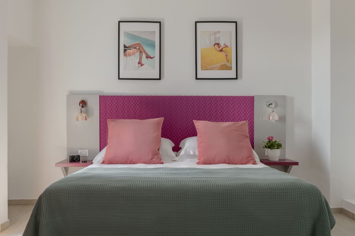 Quarto bem arrumado com uma cama, duas fotografias emolduradas na parede, uma mesa de cabeceira com uma câmera e uma pequena planta.