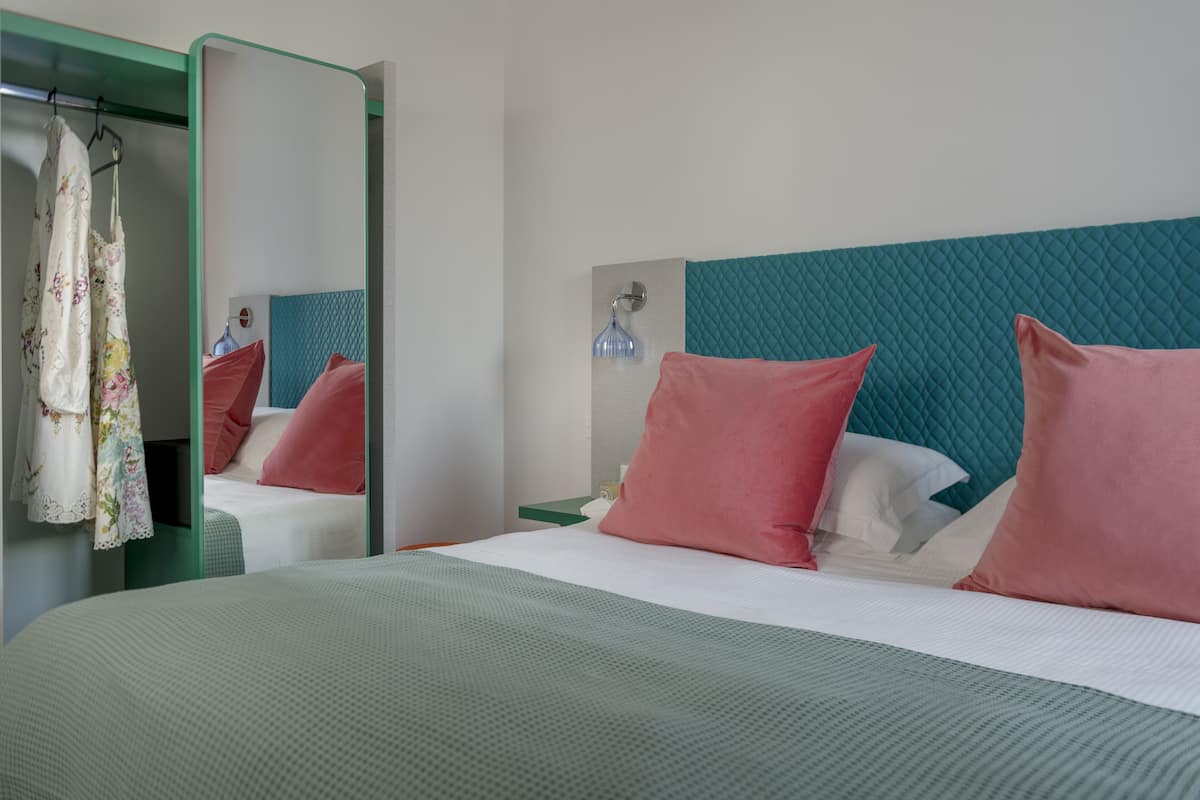 Quarto de hotel com uma cama, um espelho e um guarda-roupa.