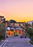 Um hotel chamado "ATALANTE" com fachada de pedra, uma varanda e uma placa com um símbolo de cartola.