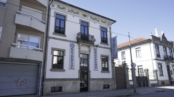 Um edifício com fachada branca, várias janelas e uma varanda com guarda-corrimão preto.