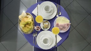Mesa de café da manhã com croissants, suco de laranja, queijo, presunto e um sachê de café Gresso.