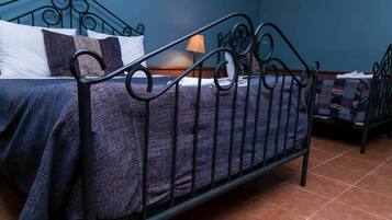Uma cama com estrutura de metal, parede azul e chão de azulejos.