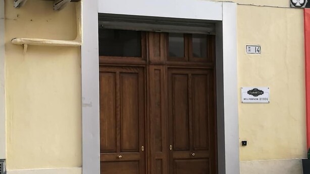Uma porta dupla de madeira com um pequeno degrau que a precede, uma caixa de serviços à esquerda e uma placa na parede à direita.