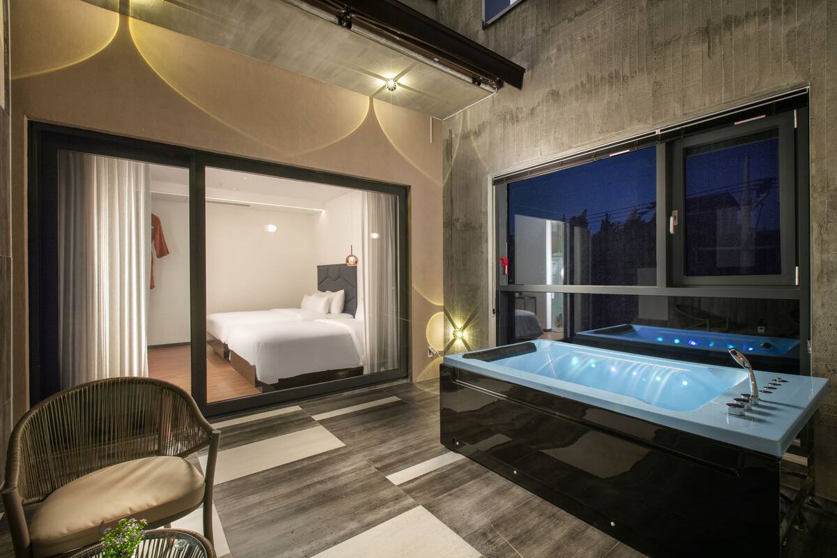 Quarto de hotel moderno com uma banheira grande, uma cama e um espaço de estar.
