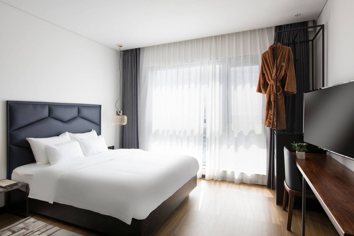 Quarto de hotel moderno com uma cama grande, uma escrivaninha com cadeira, televisão e roupão pendurado em um suporte.