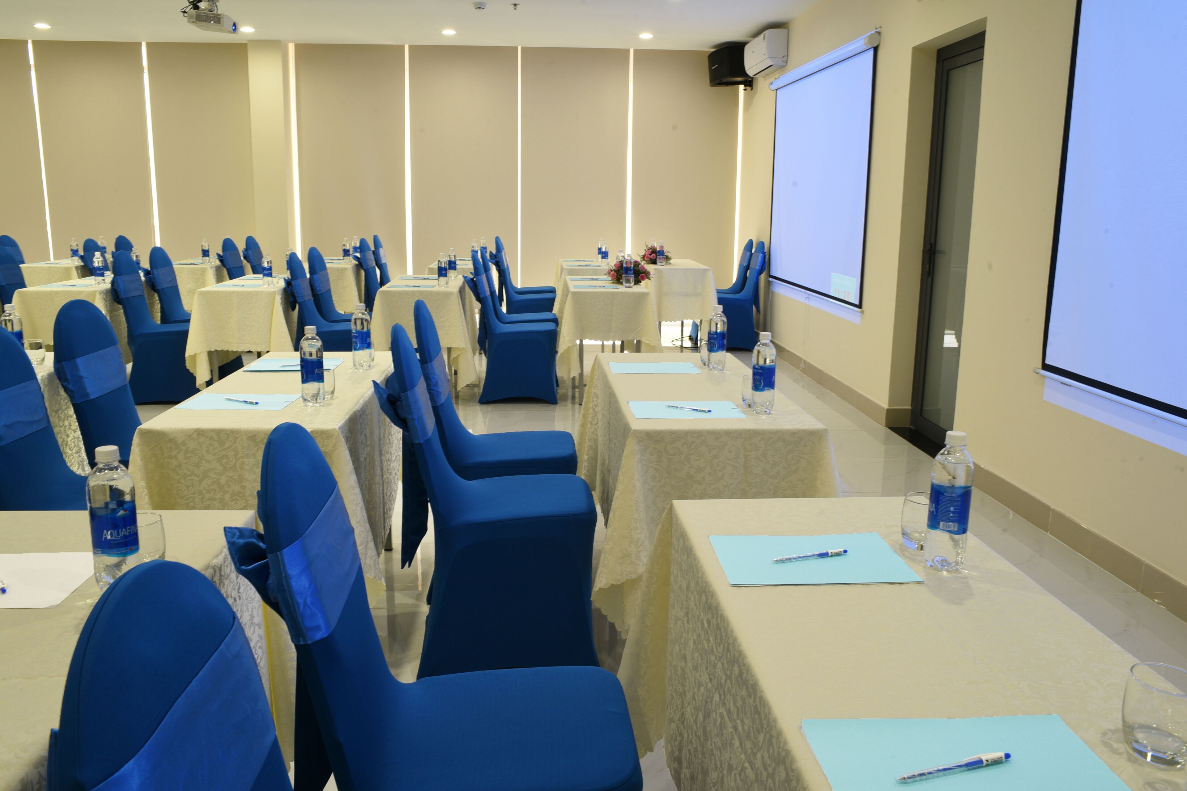 Uma sala de conferência com mesas, cadeiras e uma tela de projeção.