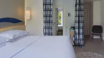 Quarto de hotel com uma cama grande, uma cadeira, banheiro com espelho e vista para o exterior.
