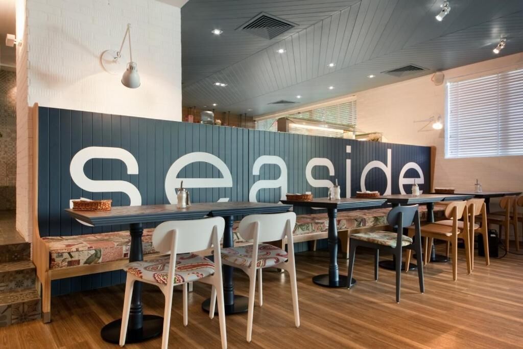 Interior de restaurante com um grande letreiro 'Seaside', mesas e cadeiras de madeira.