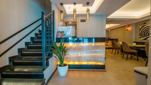 Um hall de hotel com uma receção, uma escadaria e uma área de refeições.