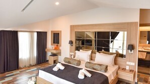 Quarto de hotel moderno com uma cama grande, uma mesa de cabeceira de madeira, uma pequena mesa de apoio e um espelho, além de uma janela com cortinas.