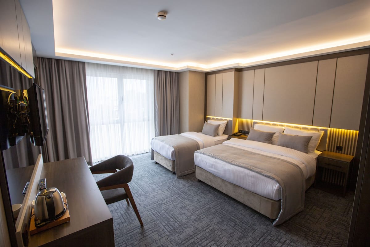 Quarto de hotel com duas camas, uma escrivaninha, uma cadeira e uma televisão.