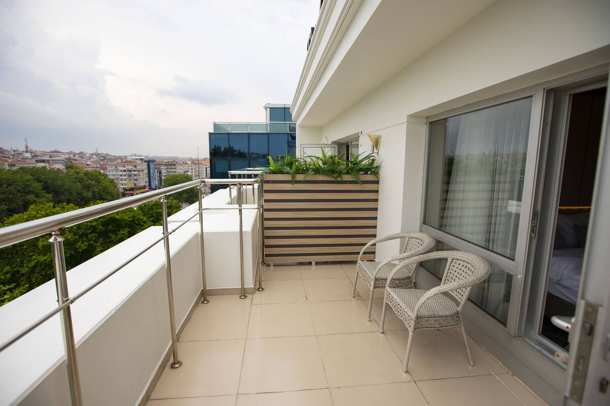 Uma varanda com vista para a cidade, uma pequena área de estar com cadeiras e um vaso com plantas.