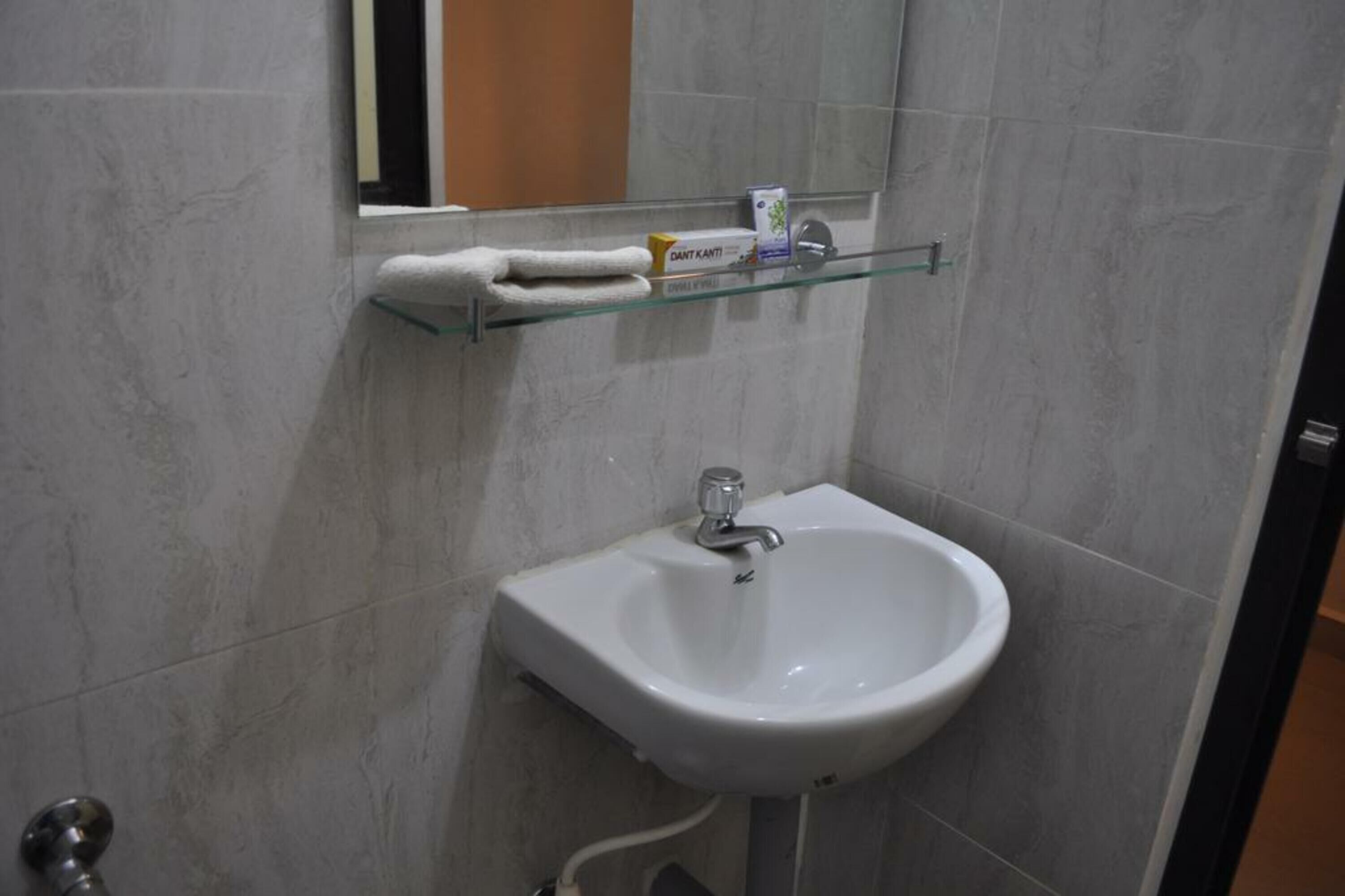Um banheiro com pia suspensa branca, prateleira de vidro com produtos de higiene e espelho sobre a pia.