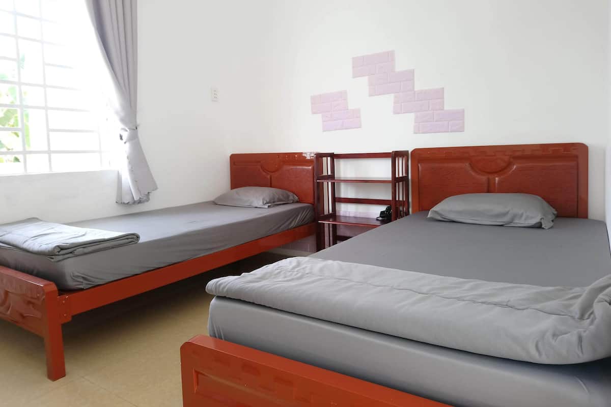 Quarto com duas camas, uma mesa de cabeceira e uma janela com cortinas.