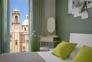 Quarto de hotel com cama, mesa de cabeceira com espelho e vista para um edifício com cúpulas e um campanário.