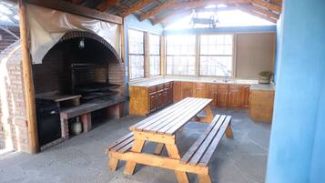 Uma cozinha rústica com forno de tijolos, armários de madeira, bancada de pedra e uma janela grande.