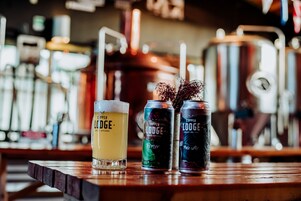 Um copo de cerveja, duas latas de cerveja e um mug de cobre em um balcão de madeira.
