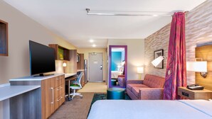 Quarto de hotel com cama, escrivaninha, televisão e banheiro visível por uma porta aberta.