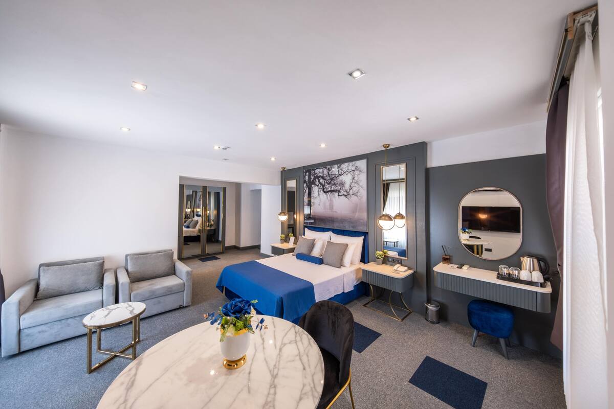 Quarto de hotel moderno com cama, dois sofás, escrivaninha e mesa redonda.
