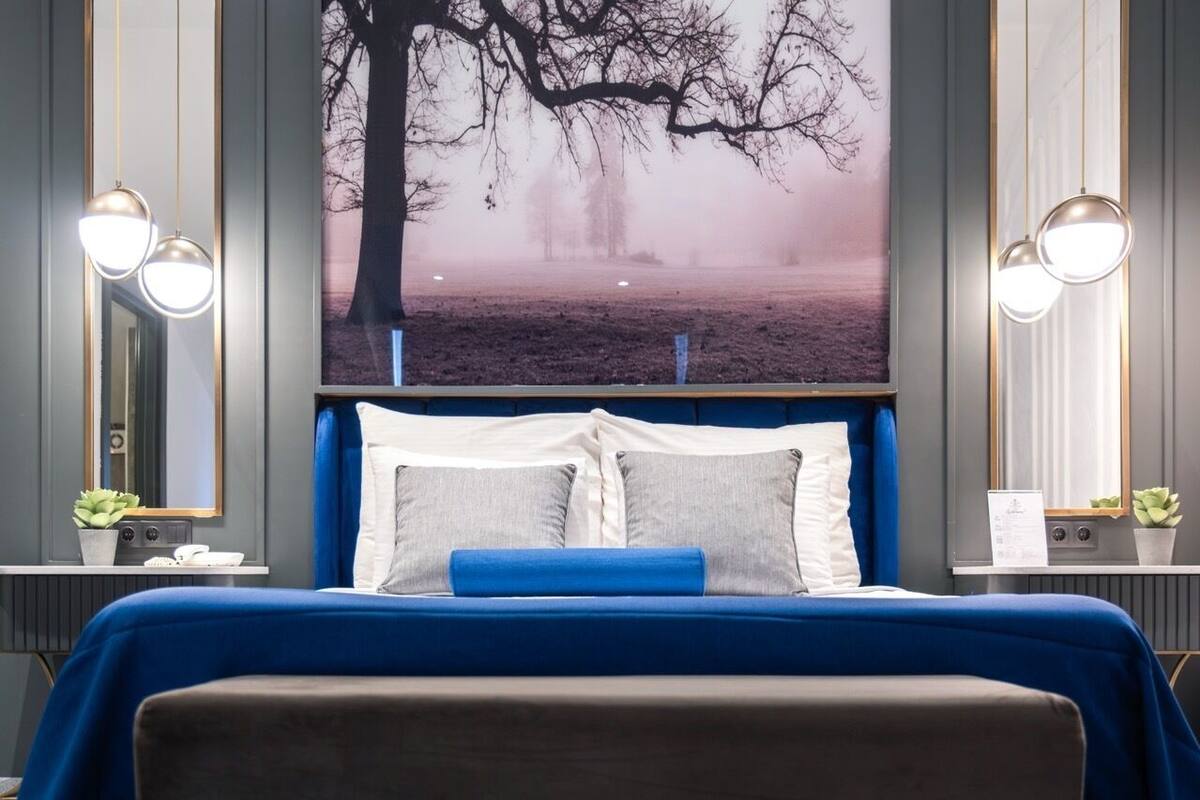 Quarto com uma cama grande, mesas de cabeceira, um espelho e uma obra de arte na parede retratando uma árvore.