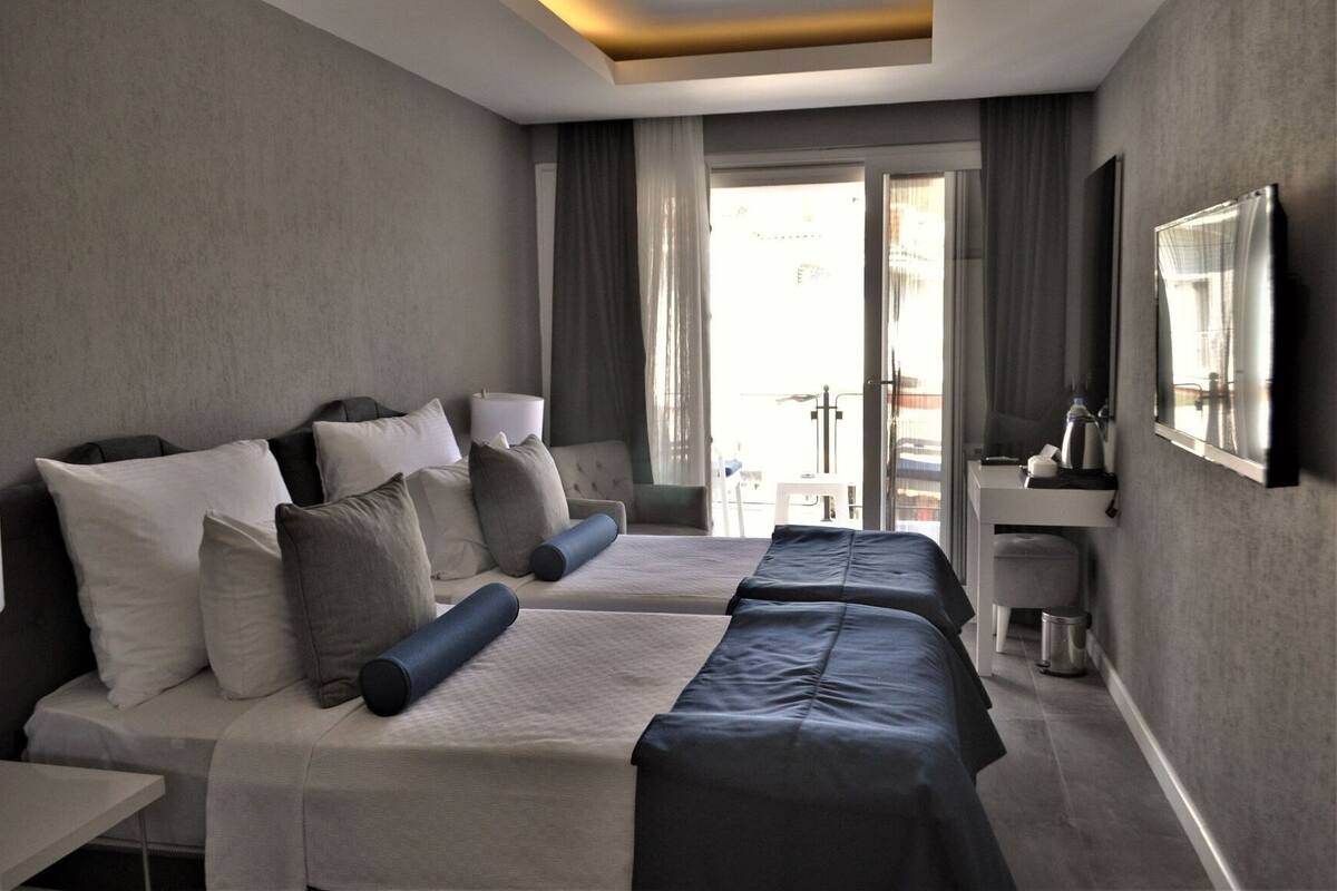 Quarto de hotel com uma cama grande, uma mesa, uma cadeira, televisão e varanda com cortinas.