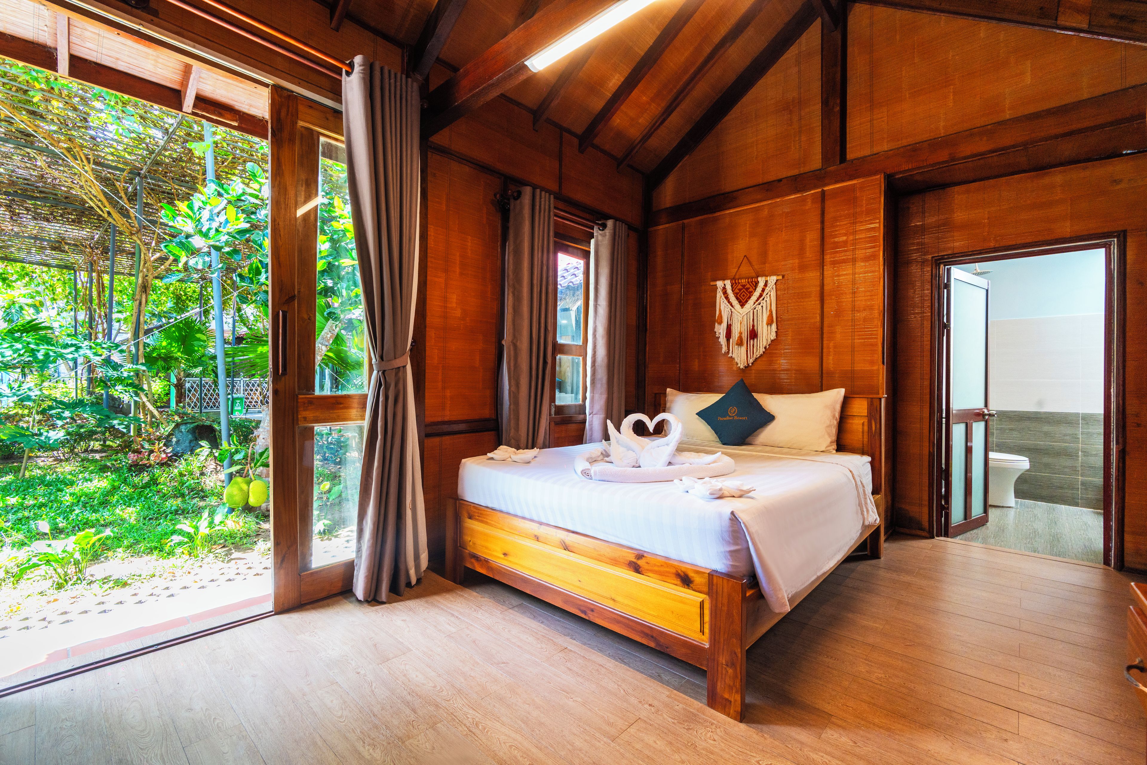 Quarto de madeira com uma cama, janela e vista para o verde.