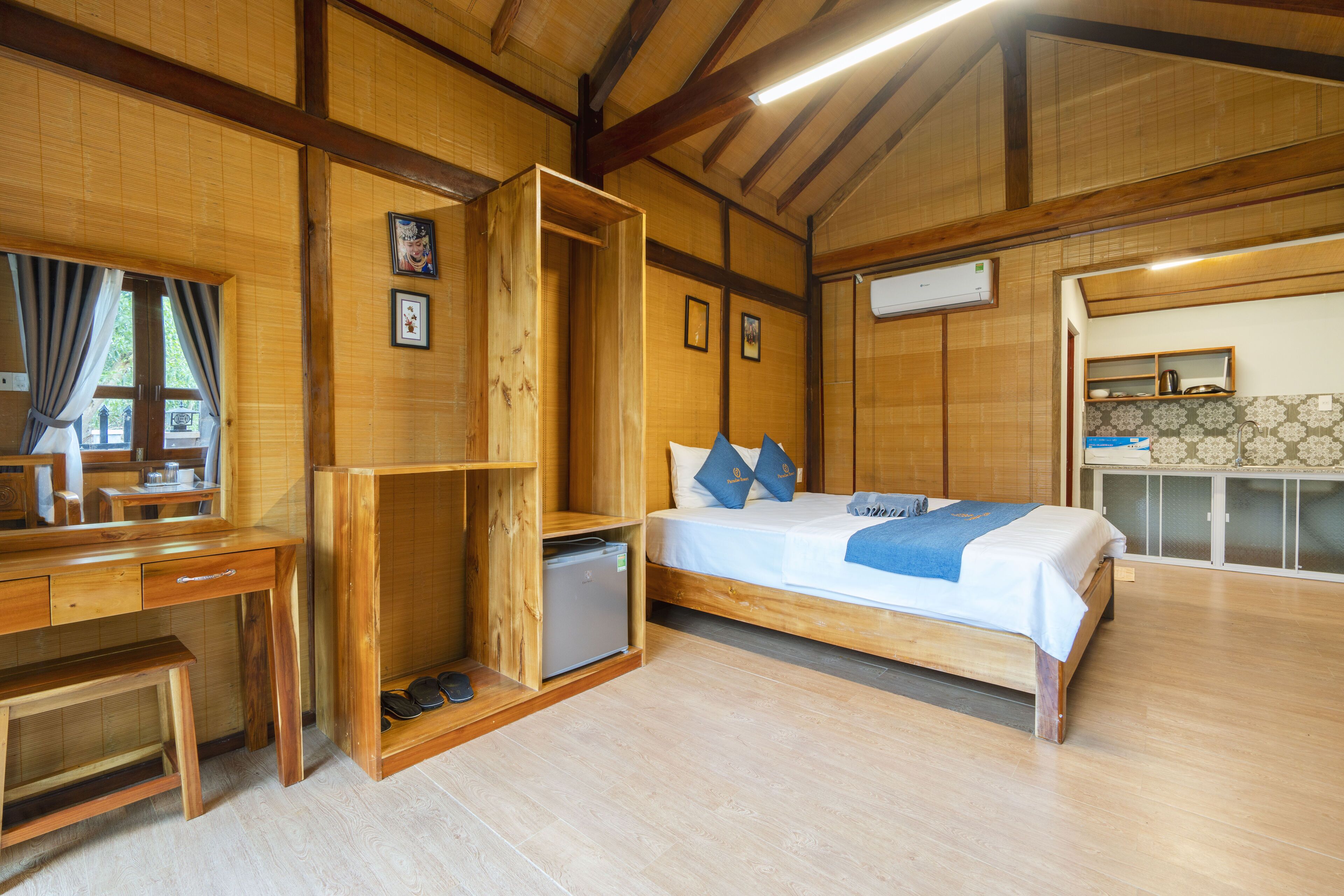 Quarto de madeira com uma cama, escrivaninha e um pequeno frigorífico.