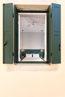 Quarto com cama, ventilador de teto e janela com persianas verdes.