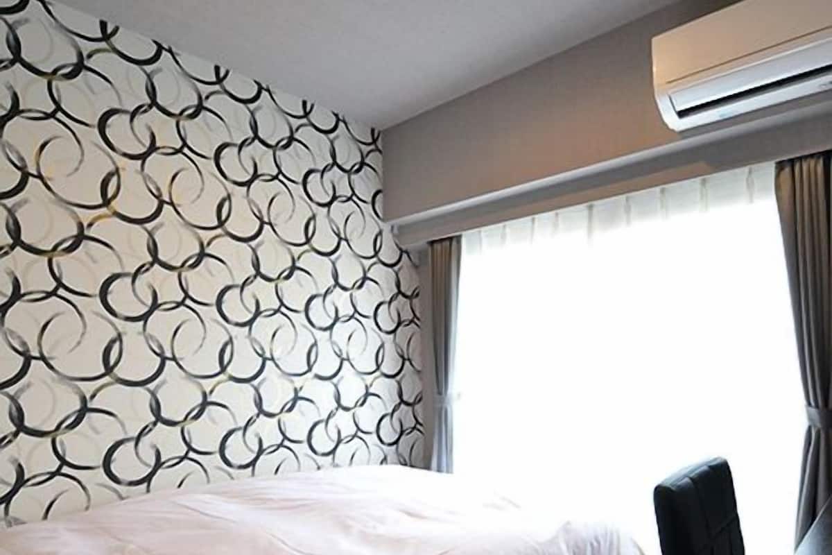 Quarto de hotel com parede estampada, uma cama, uma escrivaninha e um aparelho de ar condicionado.