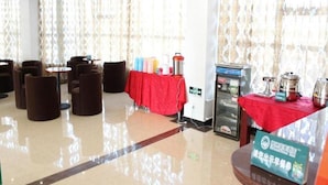 Um hall de hotel com uma mesa vermelha, cadeiras marrons e uma máquina de café.
