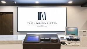 Uma receção com um ecrã digital, um monitor de computador e um terminal de pagamento no The Manga Hotel.