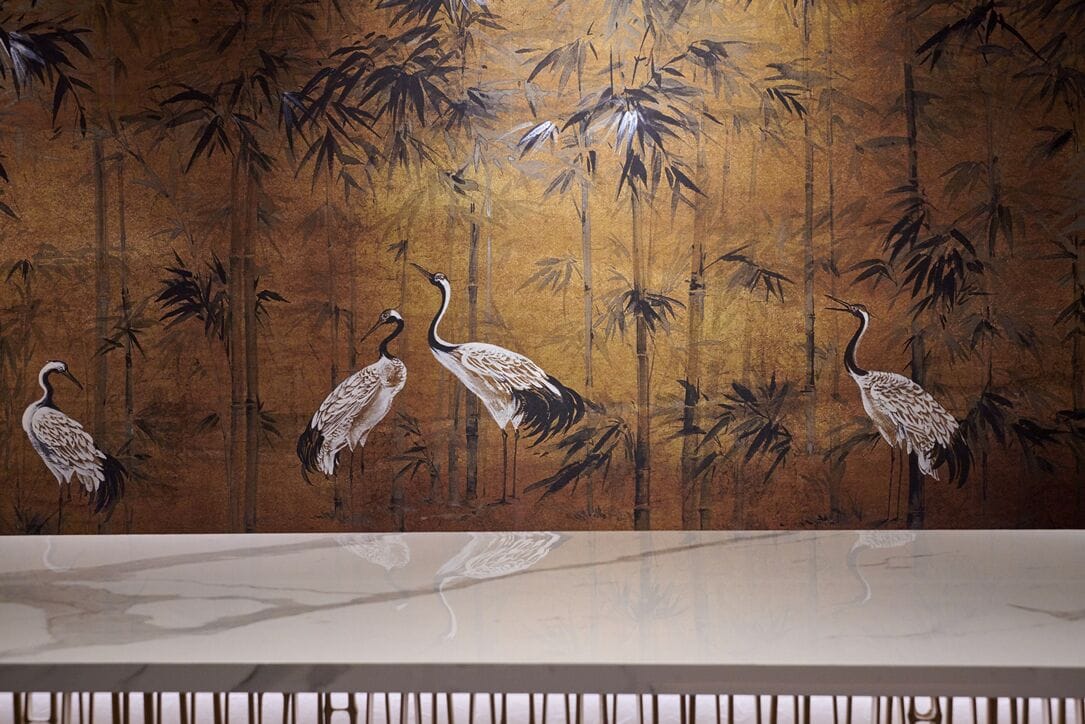 Pareda com um mural de floresta de bambu e três pássaros estilizados.