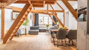 Um amplo loft com vigas de madeira aparentes, área de jantar com mesa e cadeiras, um sofá e uma cozinha com armários.