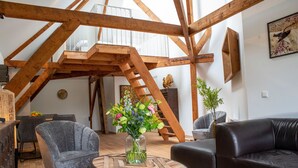 Um amplo loft com vigas de madeira aparentes, uma área de refeições com um vaso de flores e um sofá de couro preto.