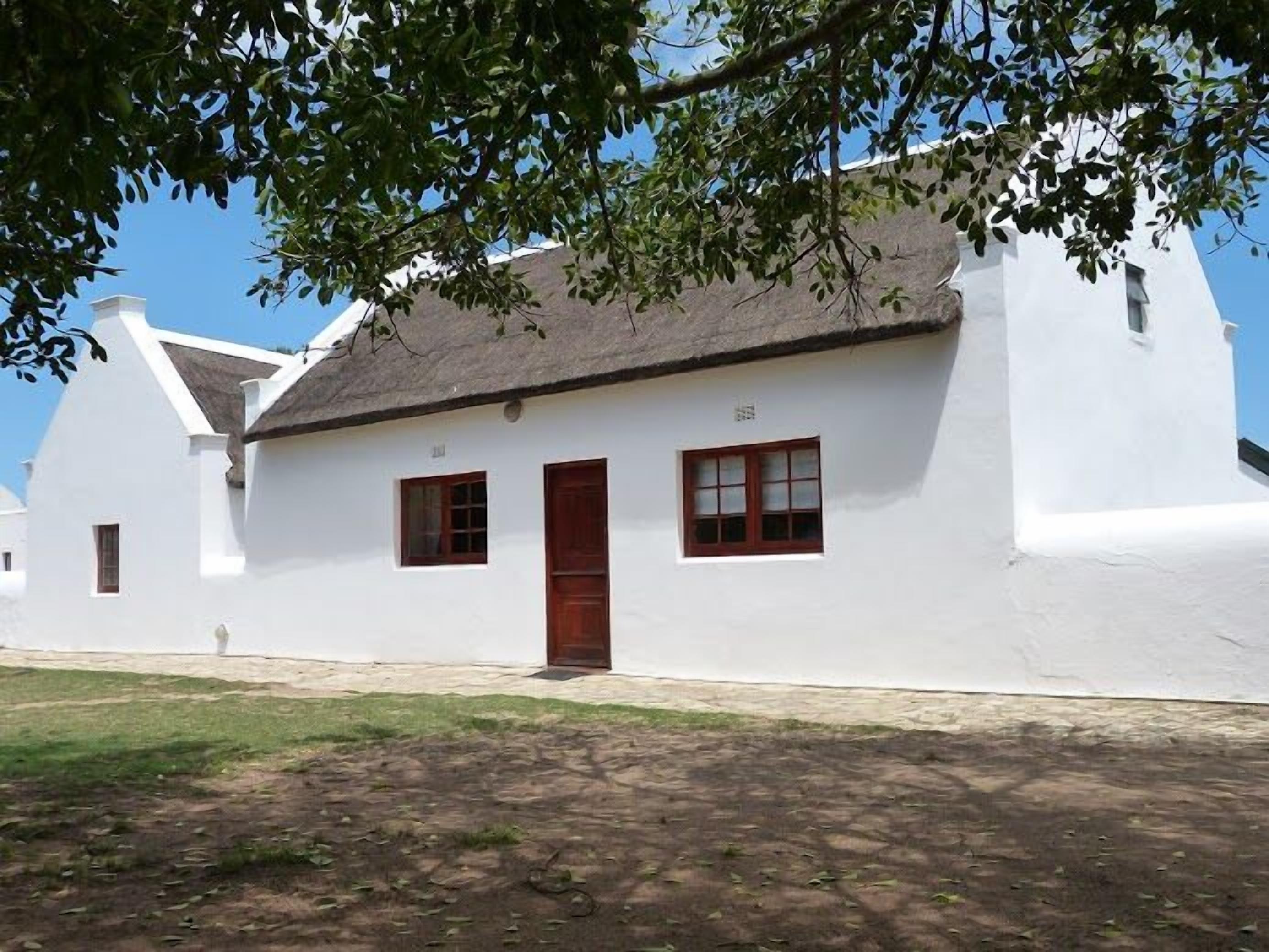 Um edifício branco com telhado de palha, porta de madeira e duas janelas com persianas.